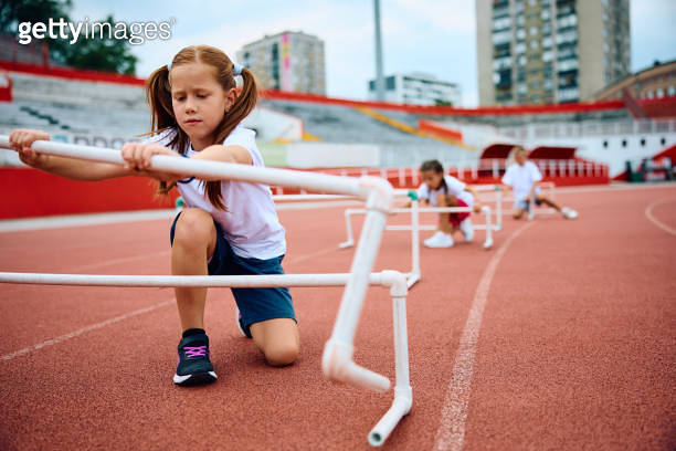 Redhead girl preparing obstacles on running track while exercising at ...