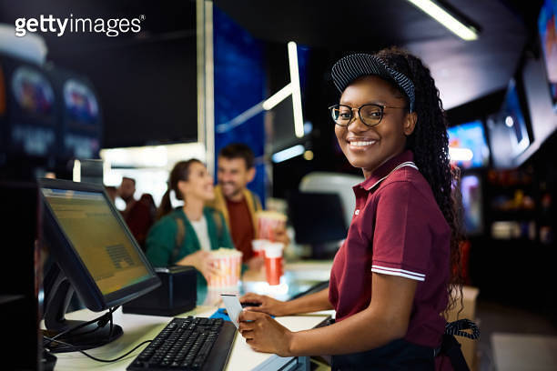 Happy black female cashier using desktop PC while working in movie ...