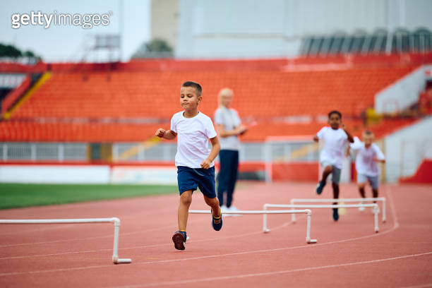 Little boy jumping over obstacles while running on a track at athletics ...