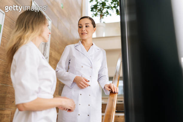 Skilled female doctor and young colleague nurse woman talking standing ...