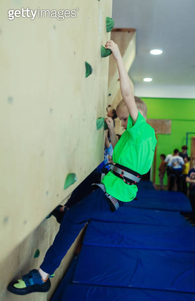 Rock climbing for children. Blond boy in a green shirt is climbing ...