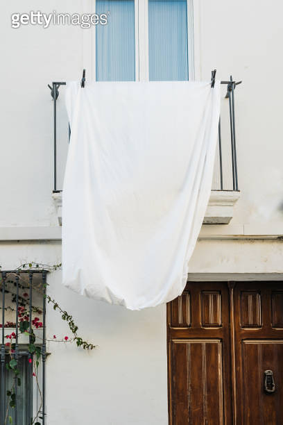 A sun-dried white sheet hangs between two blue windows above a brown ...
