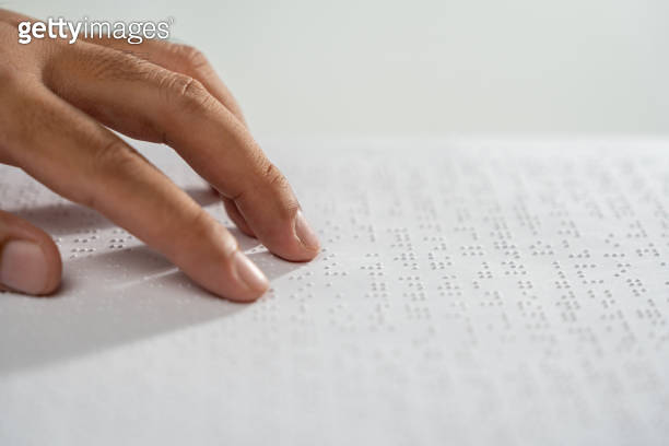 Hand of a blind person reading some braille text on page paper to learn ...
