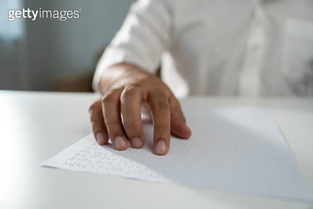 Hand of a blind person reading some braille text on page paper to learn ...