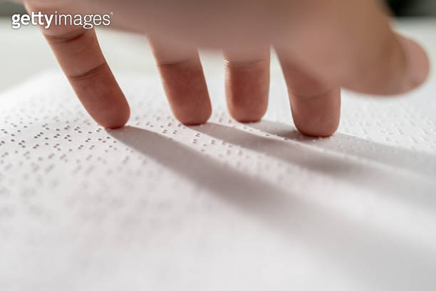 Hand of a blind person reading some braille text on page paper to learn ...