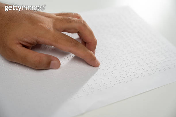 Hand of a blind person reading some braille text on page paper to learn ...