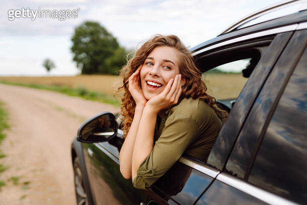 Young woman hanging out of car with hands up enjoying fresh summer wind ...