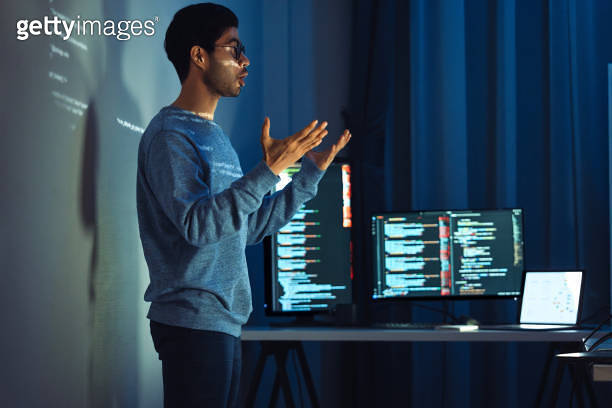 Indian man programmer standing in front of a screen with code projected ...