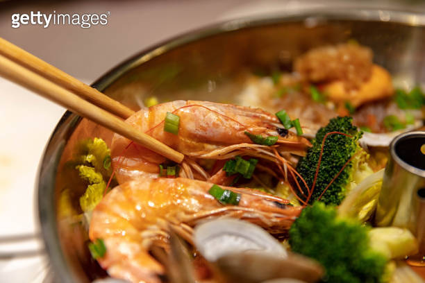 Chinese seafood hot pot with shrimp and scallops, a shrimp picked up ...