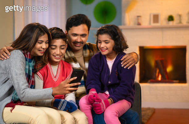 Joyful parents with kids using mobile phone with winter wear at home ...