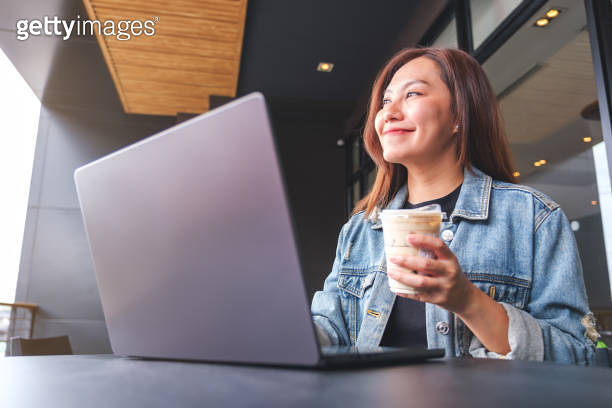 Portrait image of a young woman drinking coffee while working on laptop ...