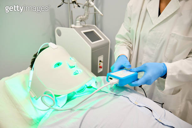 A person is getting a facial treatment with a green light led mask. 이미지 ...