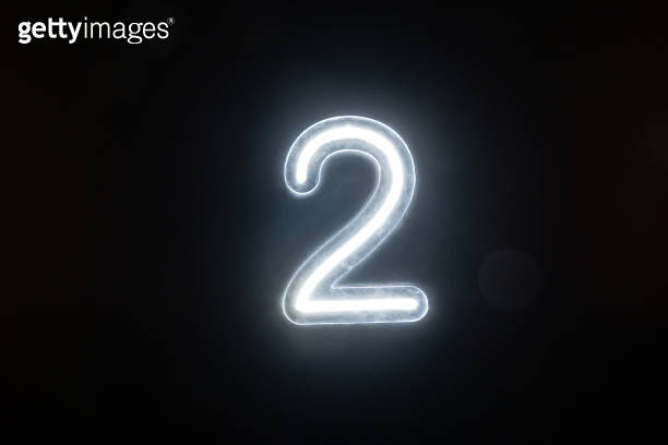Number two glowing on the dark background. Close up of bright number 2 ...