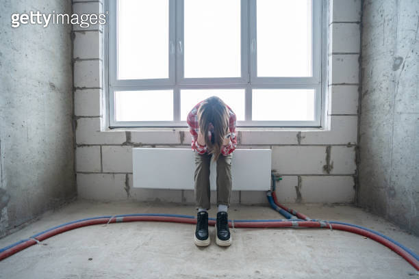 Upset woman sitting on a radiator and holding her head in hands in an ...