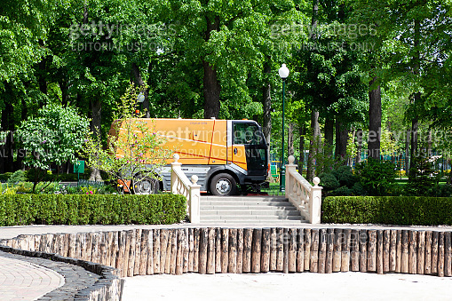 An orange street sweeper in a green park setting, surrounded by lush ...
