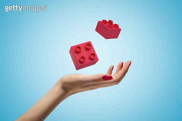 Female hand throwing two red lego pieces up in the air on blue ...