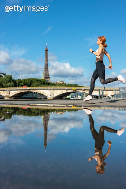 Middle-aged woman taking up outdoor activities, jumping over puddles at ...