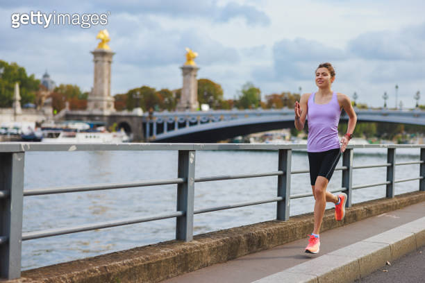 Active young woman in sports outfit running on promenade by the Seine ...