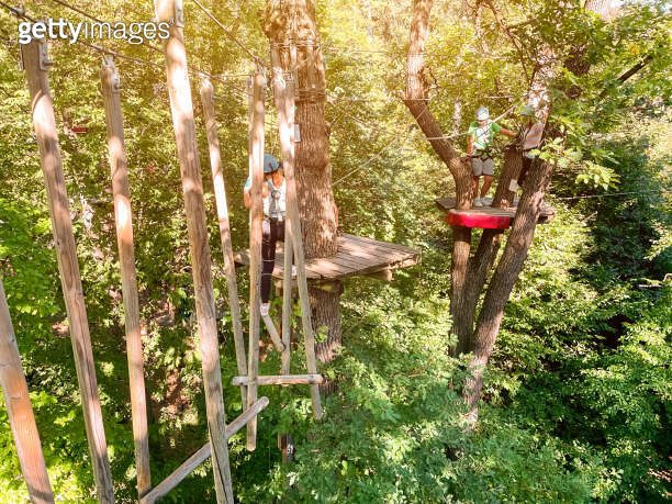 A group of people goes on hinged trail in extreme rope Park in summer ...