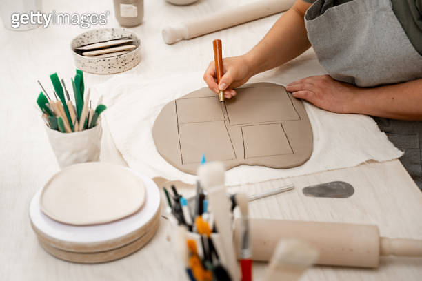 Cutting out figures from a flat sheet of clay with a sculpting tool ...