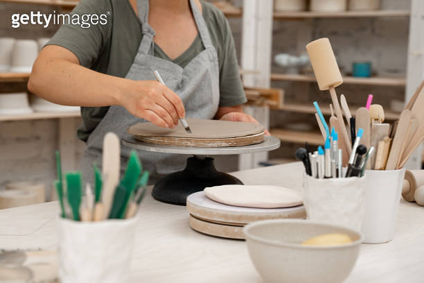 Girl is modeling clay into a round form. Using a sharp pottery carving ...