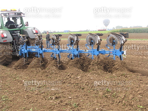 a tractor with a big swivel plow is two way plowing in the clay soil in ...