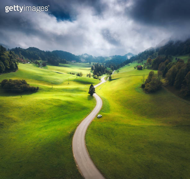 Aerial view of country road in green alpine meadows on overcast summer ...