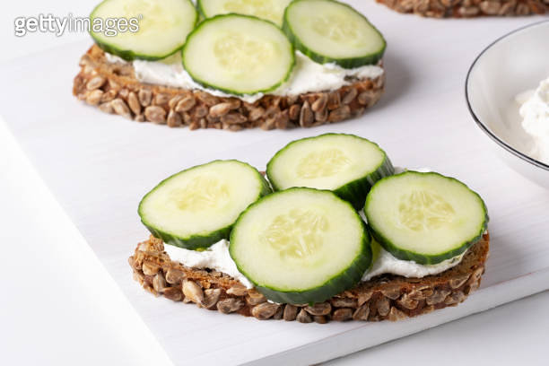 Rye bread with cream cheese and cucumbers on a white table. Whole grain ...