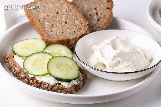 Rye bread with cream cheese and cucumbers on a white table. Whole grain ...