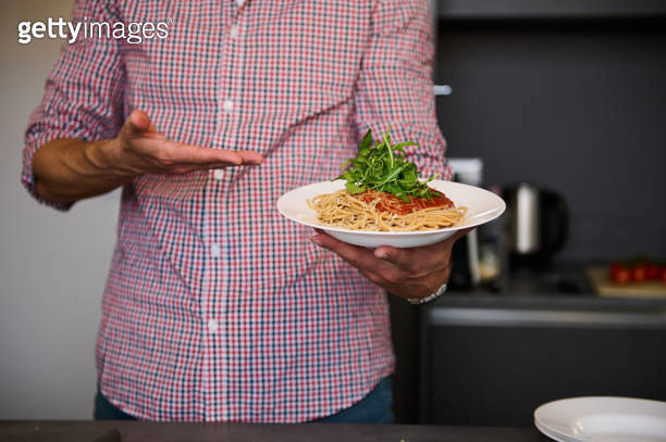 Close-up hands of young Italian chef showing white plate with Italian ...