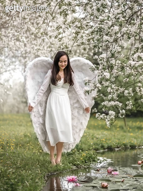 A beautiful woman angel stands in a blooming apple orchard. Spring ...