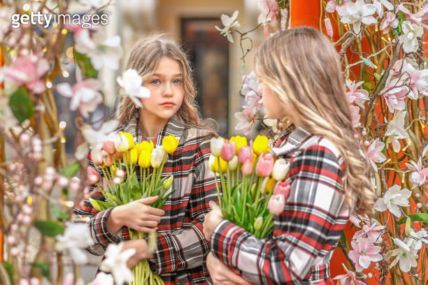A teenage girl stands at a mirror on the street with tulips. Spring ...