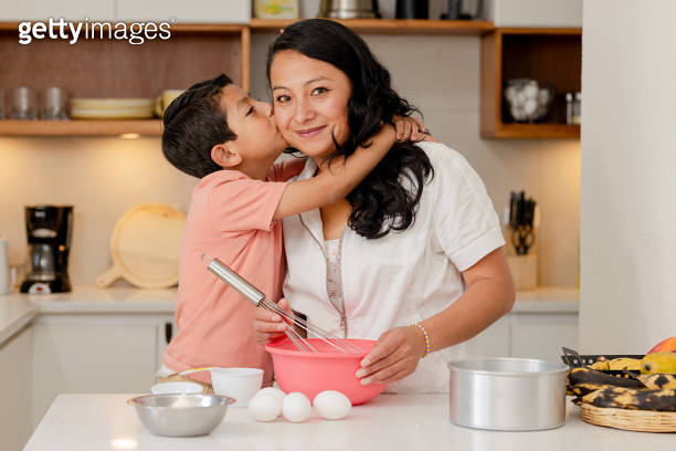 Hispanic mom and son cooking at home-son giving mom a kiss-mom teaching ...