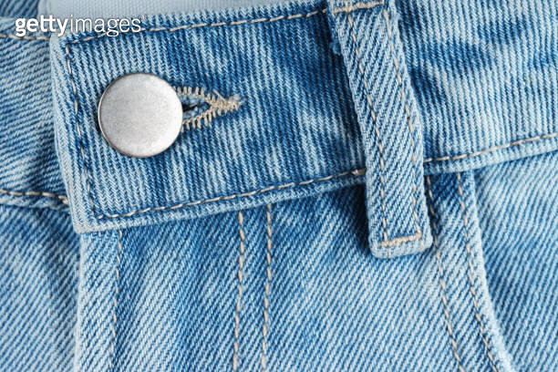 Metal button, belt loop with decorative seams of blue denim jeans close ...