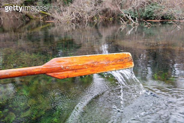 Closeup of oar paddle from row boat moving in water on green lake with ...