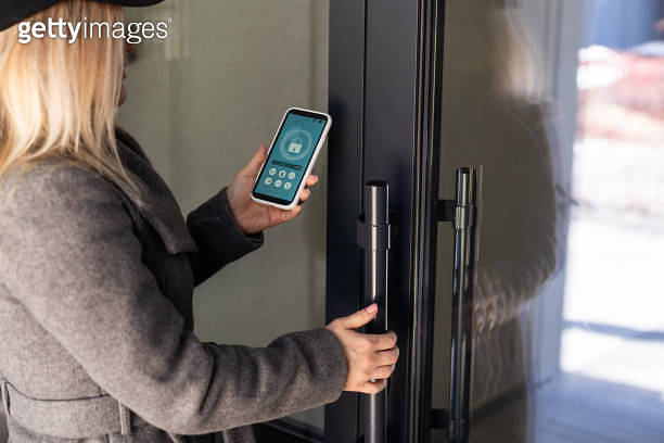Woman locking smartlock on the entrance door using a smart phone ...