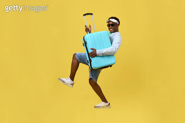 Funny African guy holding big blue suitcase by handle in hand stepping ...