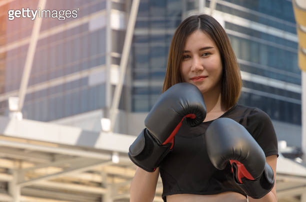 Portrait of young female boxer in black boxing gloves standing in front ...