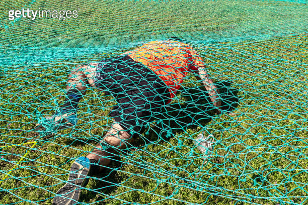 an athlete crawling under a net at an obstacle course race, ocr race ...