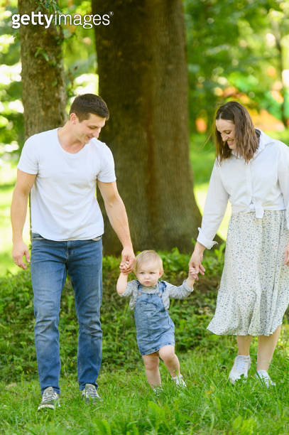 Toddler goes for walk outdoors in park with his parents, holding hands ...