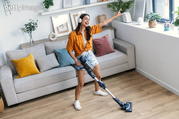 Young happy woman listening and dancing to music while cleaning the ...