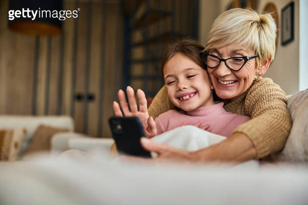A smiling grandma and her grandchild talking to someone over the video ...