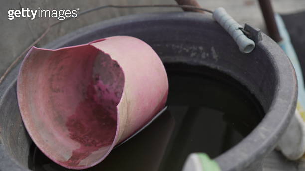 A red broken ladle floats in a black plastic bucket filled with water ...