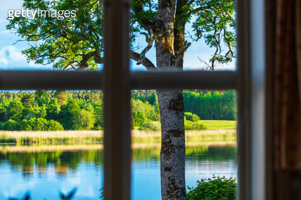 Beautiful view through a window of a serene lake with lush green trees ...
