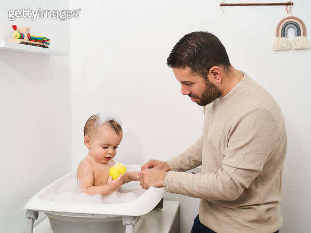 a man bathing his son playing with a toy in the bathtub with a lot of ...