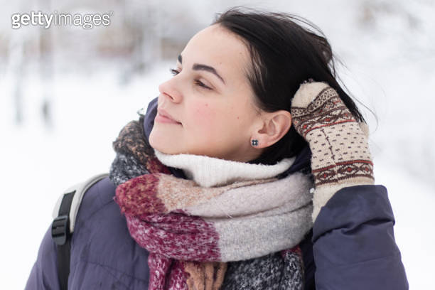 Young smiling beautiful woman wearing scarf outdoors during snowfall ...
