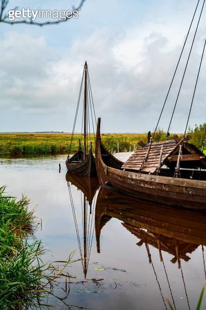 wooden Viking ships docked on a calm river with a scenic view of the ...