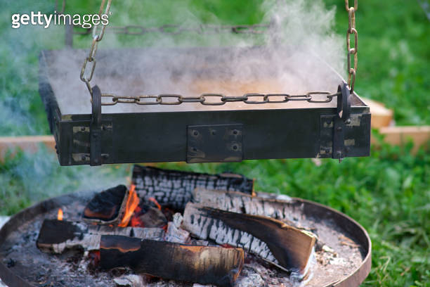 A metal pan with a chain hanging from it over a fire. The pan is filled ...