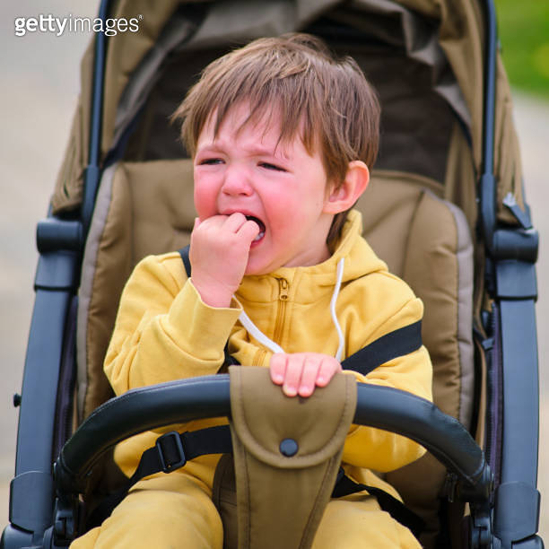 The young child is crying while sitting in the baby stroller during a ...