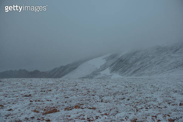 Stones and frozen grasses on snow-covered stony pass against snowy ...
